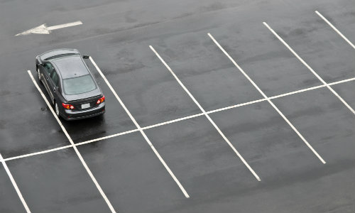 a single car parked on an asphalt parking lot within lanes